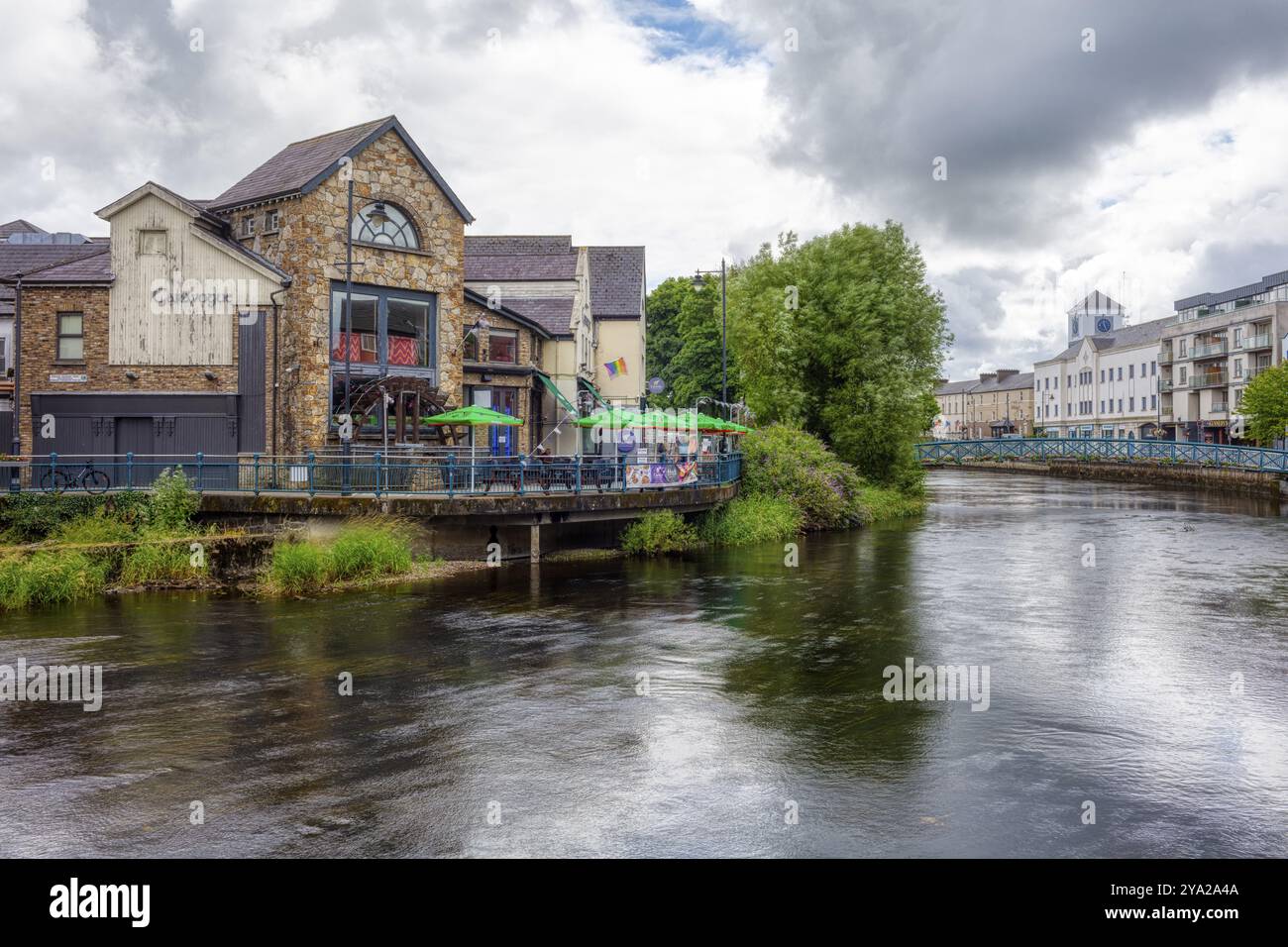 Historic buildings and cafes along a river with green vegetation and ...