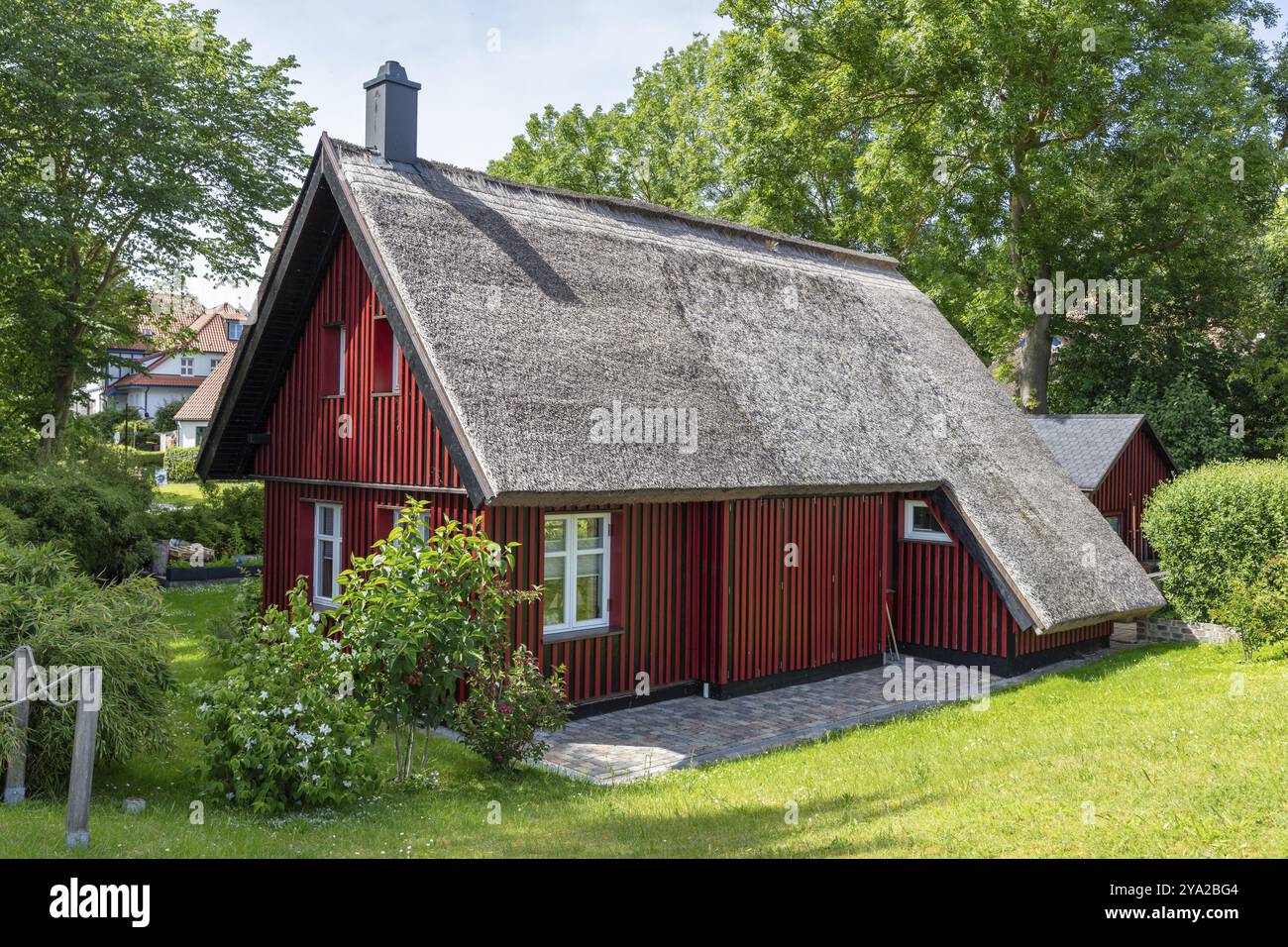 Traditional red country house with thatched roof in a green garden area ...