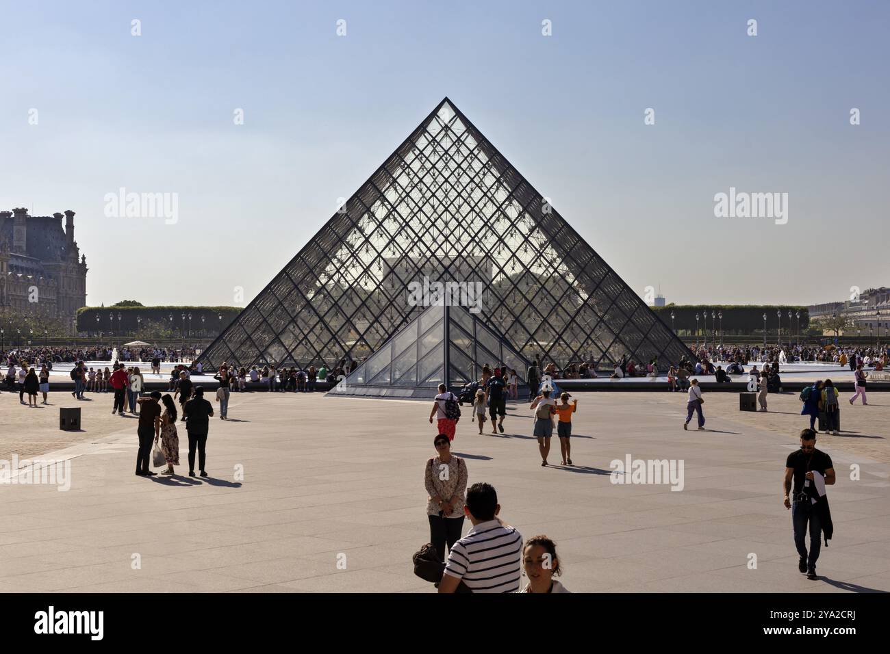 People stroll around the modern glass pyramid of the Louvre on a sunny ...