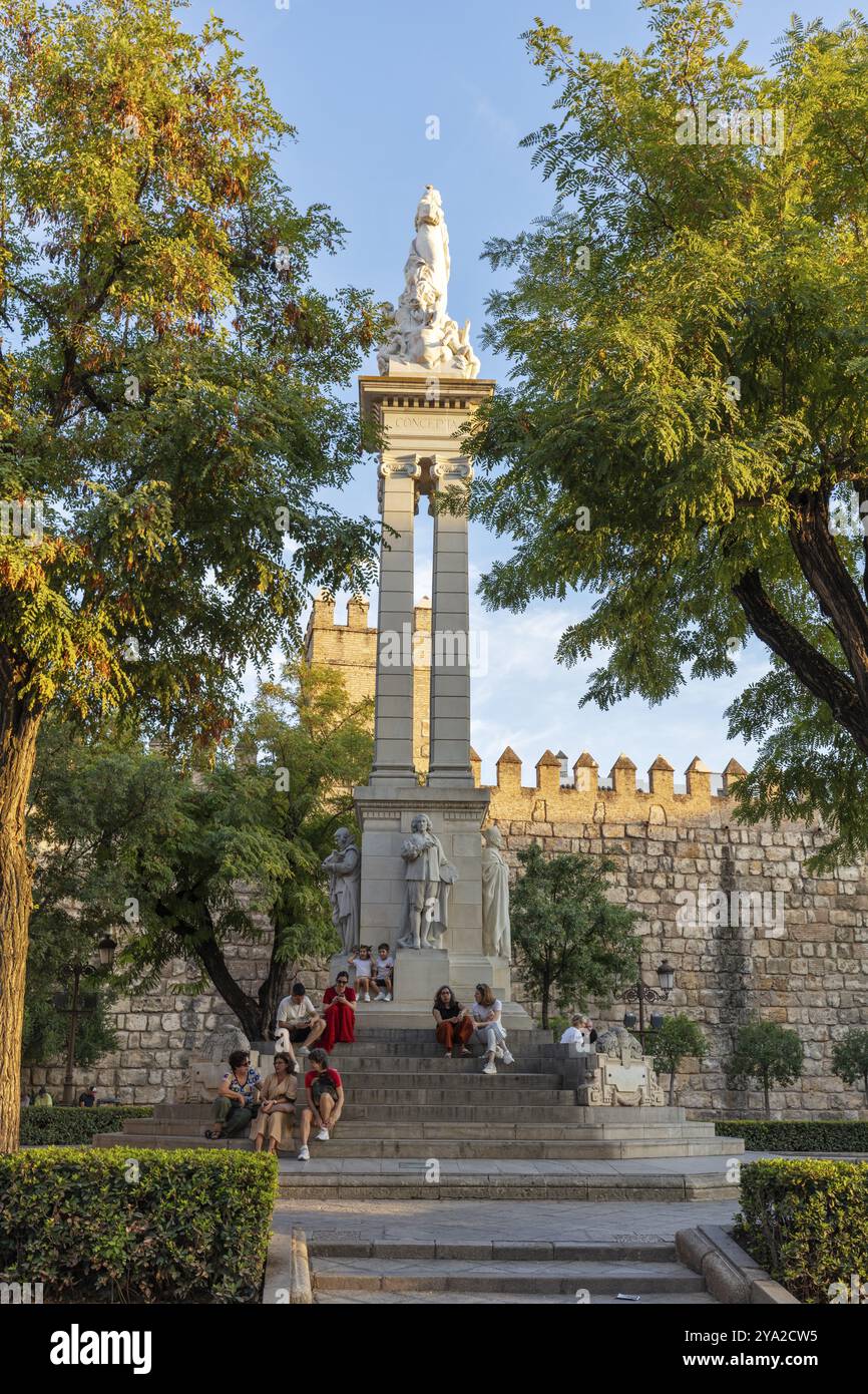 Monument with statues surrounded by trees and people at dusk, Seville ...