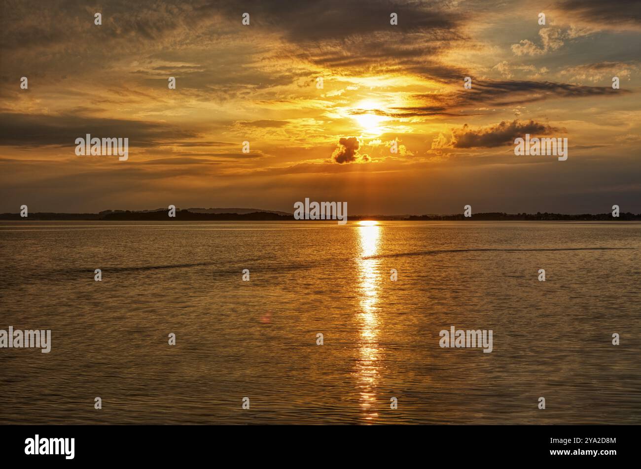 A bright orange sunset is reflected on the surface of the water ...