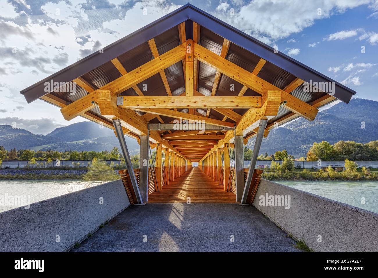 Wooden bridge with roof, flooded with sunlight, with mountain backdrop ...