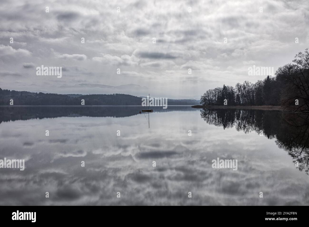 A calm lake with a single boat in the water, surrounded by forest and a ...