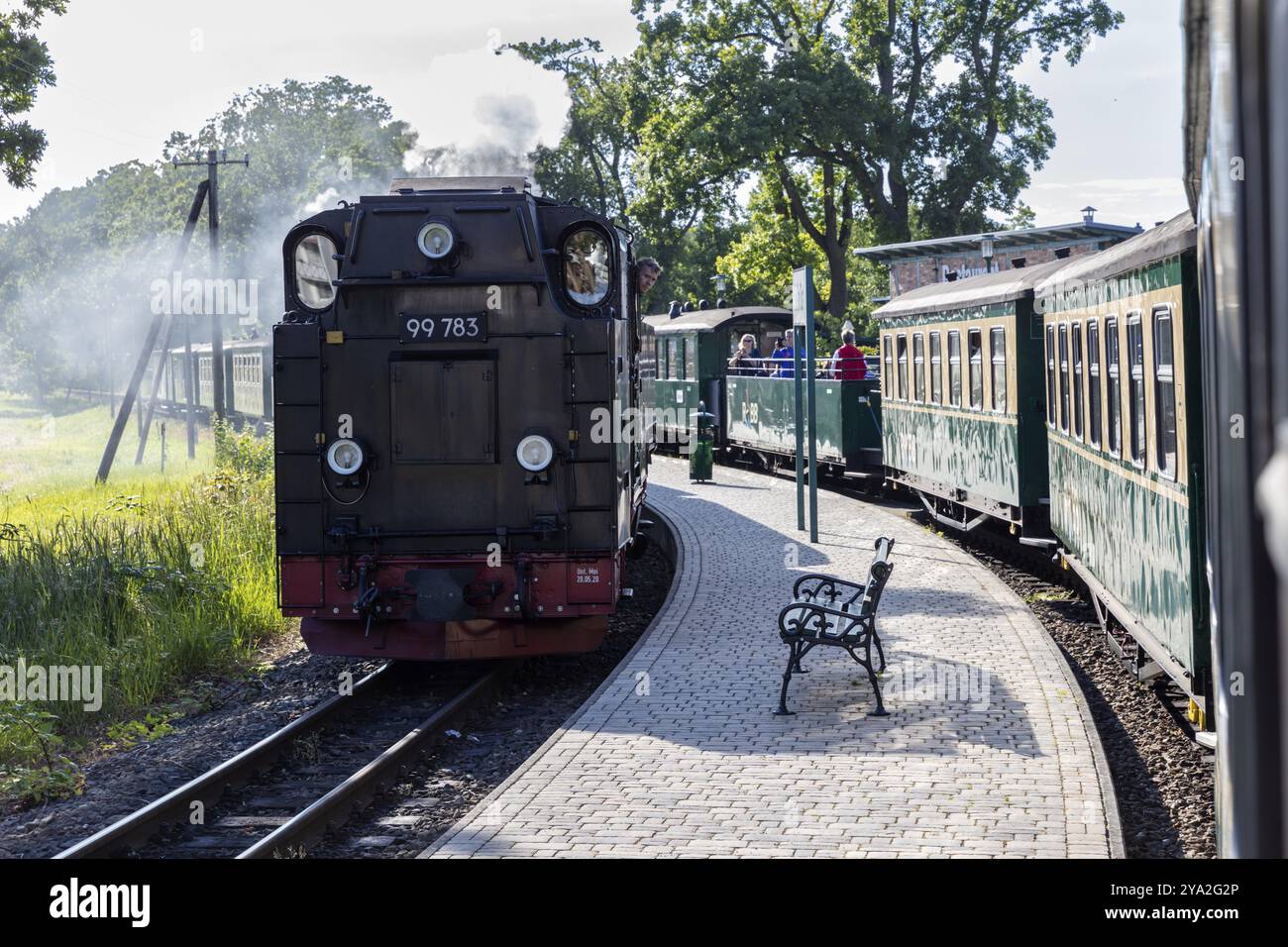 A steam locomotive pulling wagons, shot from behind on a sunny platform ...