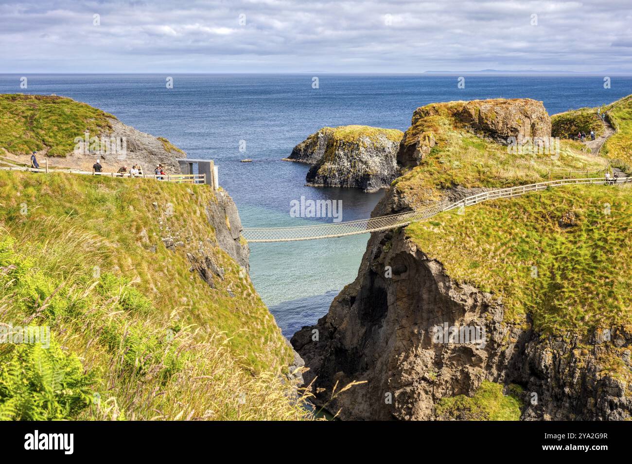 A suspension bridge connects two rocky cliffs with a picturesque sea ...
