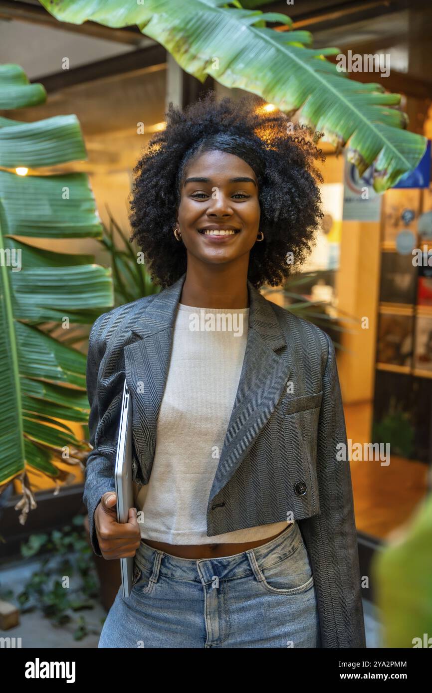 Vertical portrait of a happy african woman holding laptop at the ...