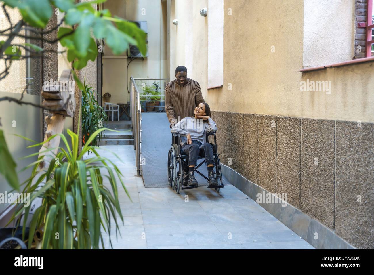 African man pushing wheelchair of disabled friend along a ramp outside ...