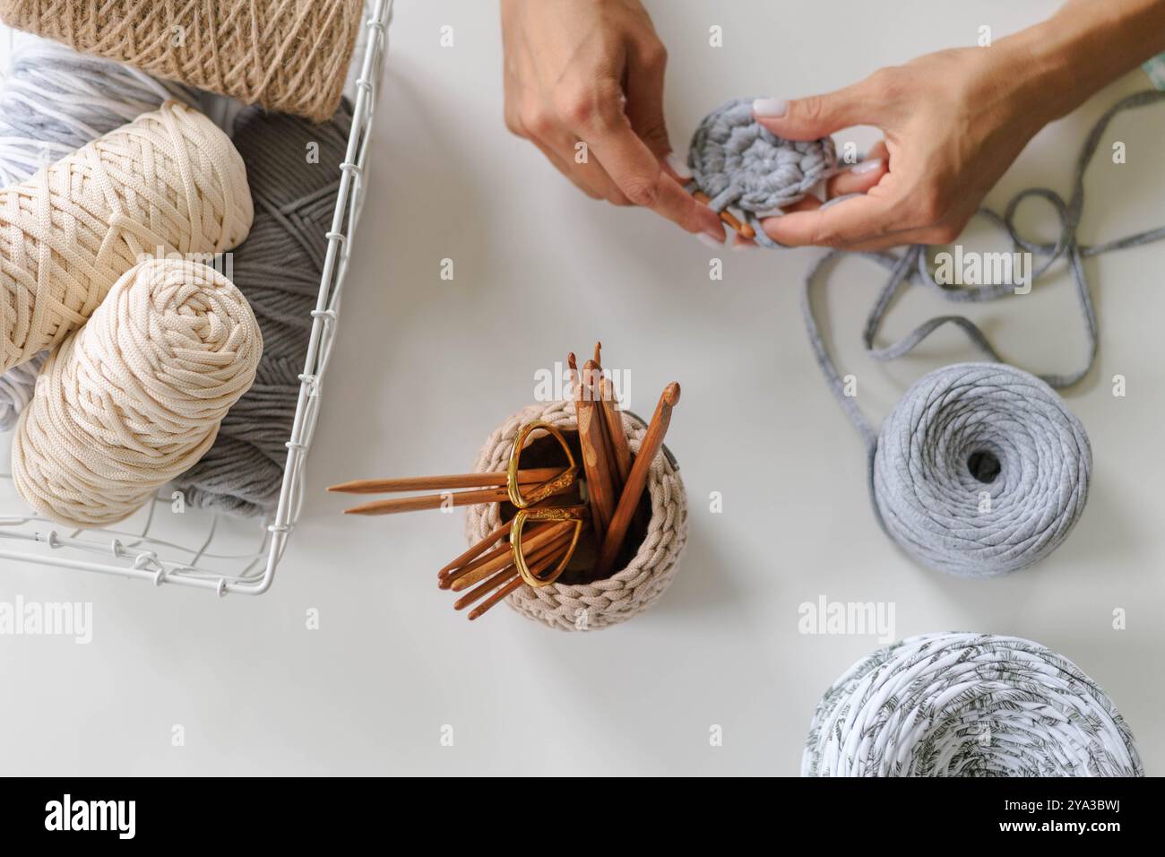 Women's hands crochet with gray yarn on a white background. Skeins of ...
