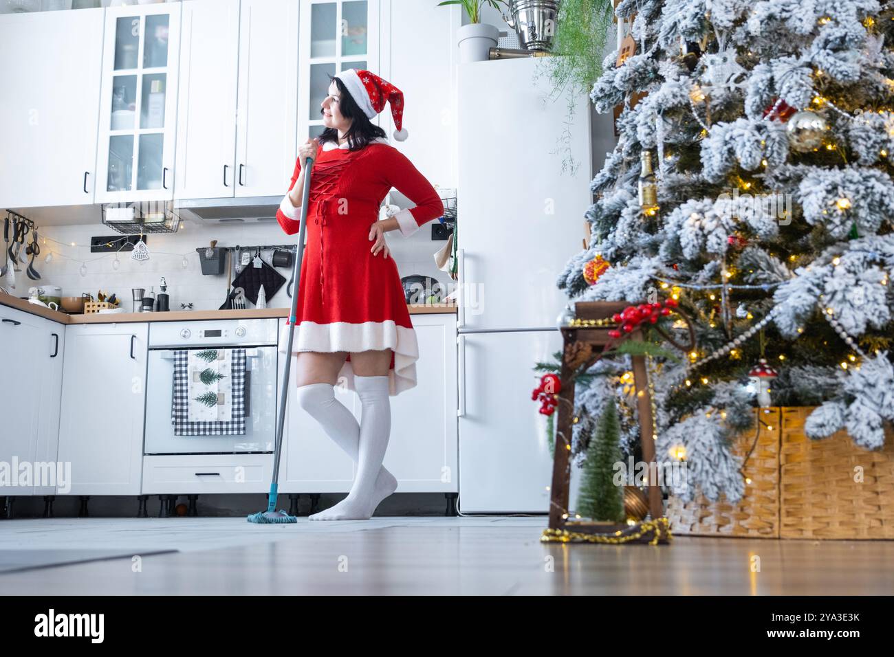 A woman in a red dress and Santa hat cleans the floor with a mop in a ...