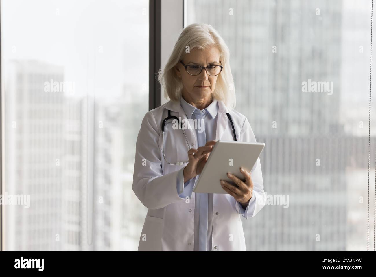 Serious older age female doctor cardiologist look on tablet screen ...