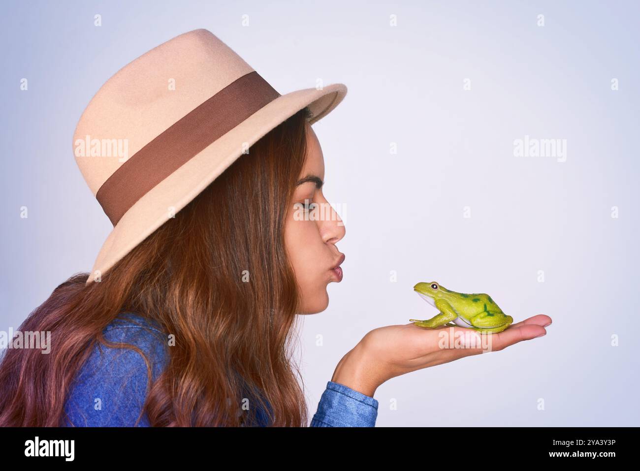 Face, frog and profile of woman kissing in studio on blue background ...