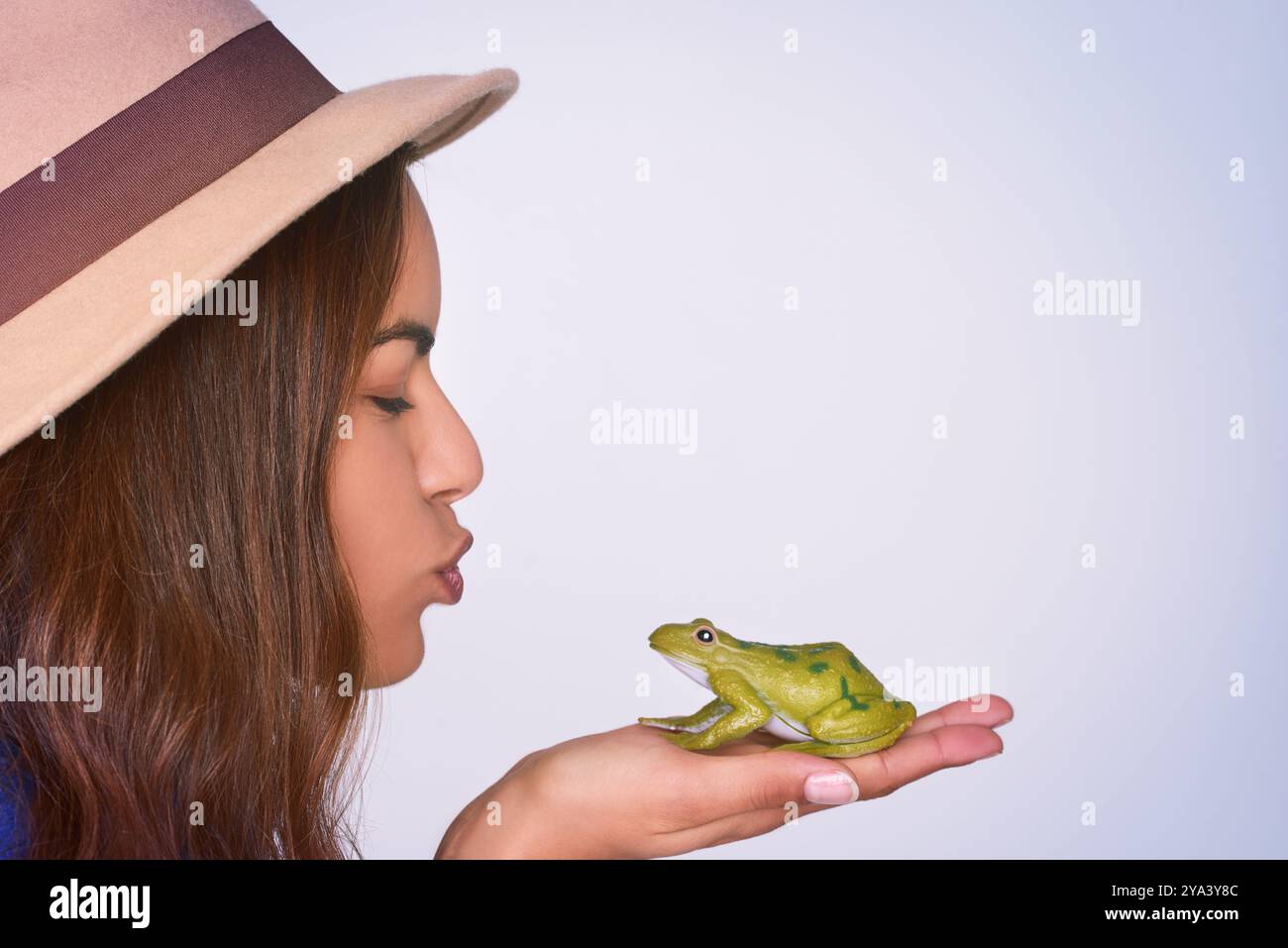 Face, kiss and profile of woman with frog in studio on blue background ...