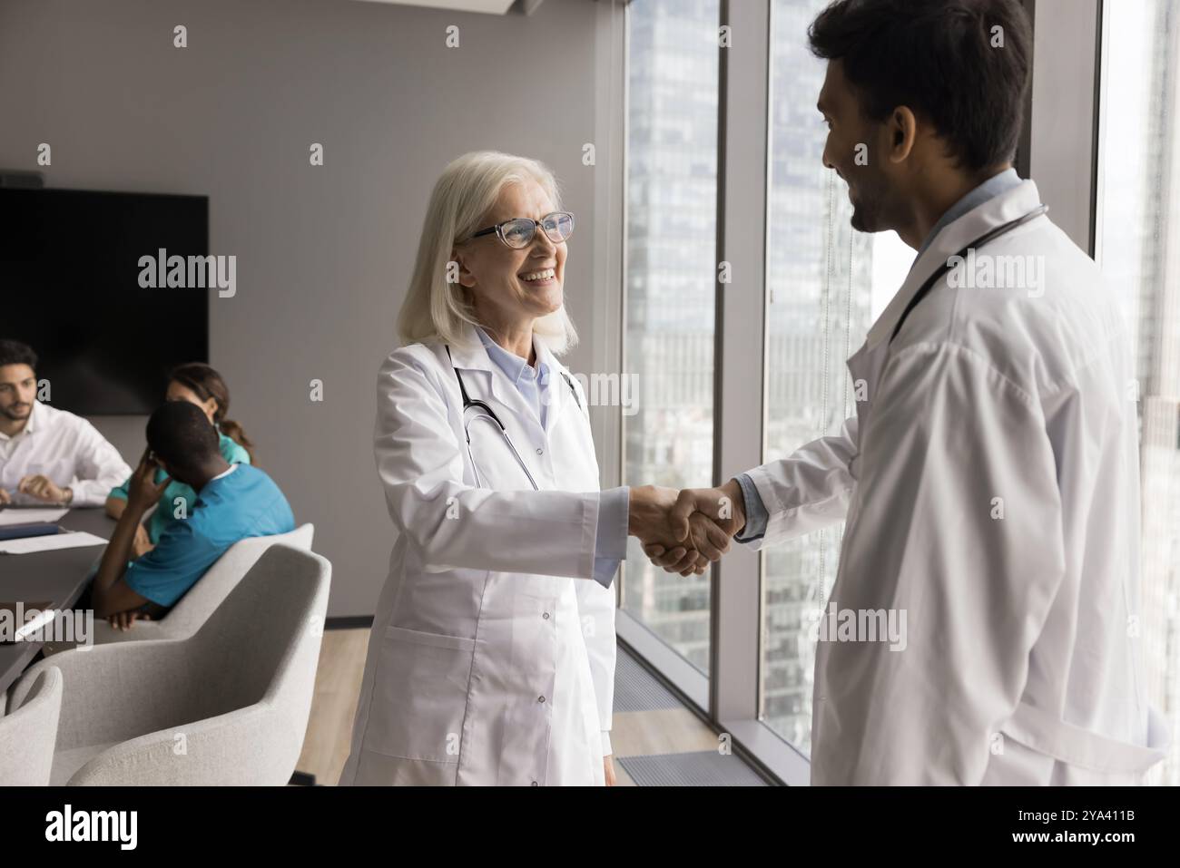 Friendly senior female chief physician handshake with millennial male ...