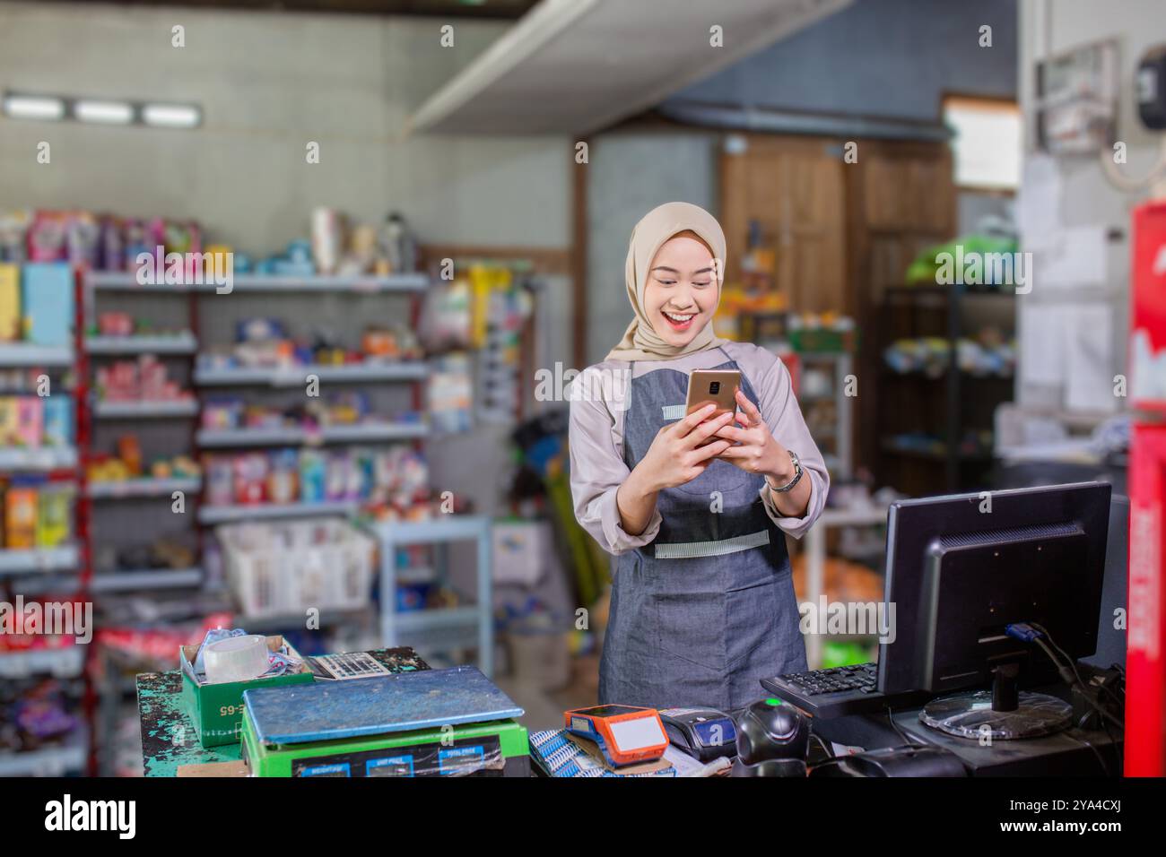 A smiling female cashier is engaged with her smartphone inside a ...