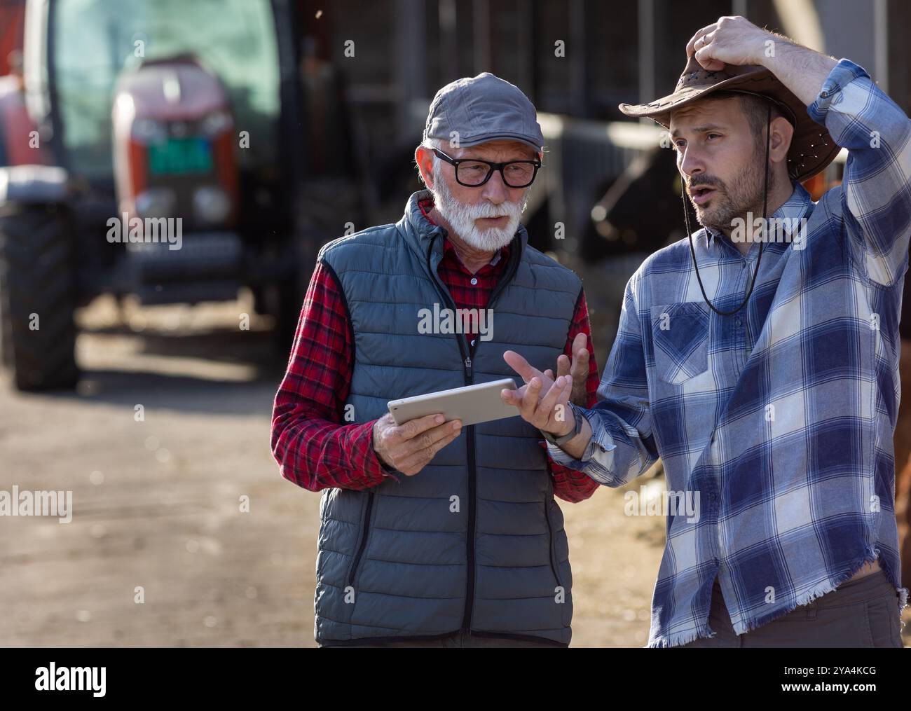 Two farmers talking in front of cowshed and tractor in background on ...