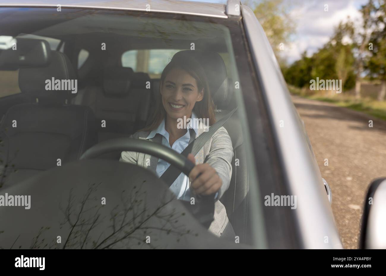Cheerful pretty business woman driving car on countryside road ...