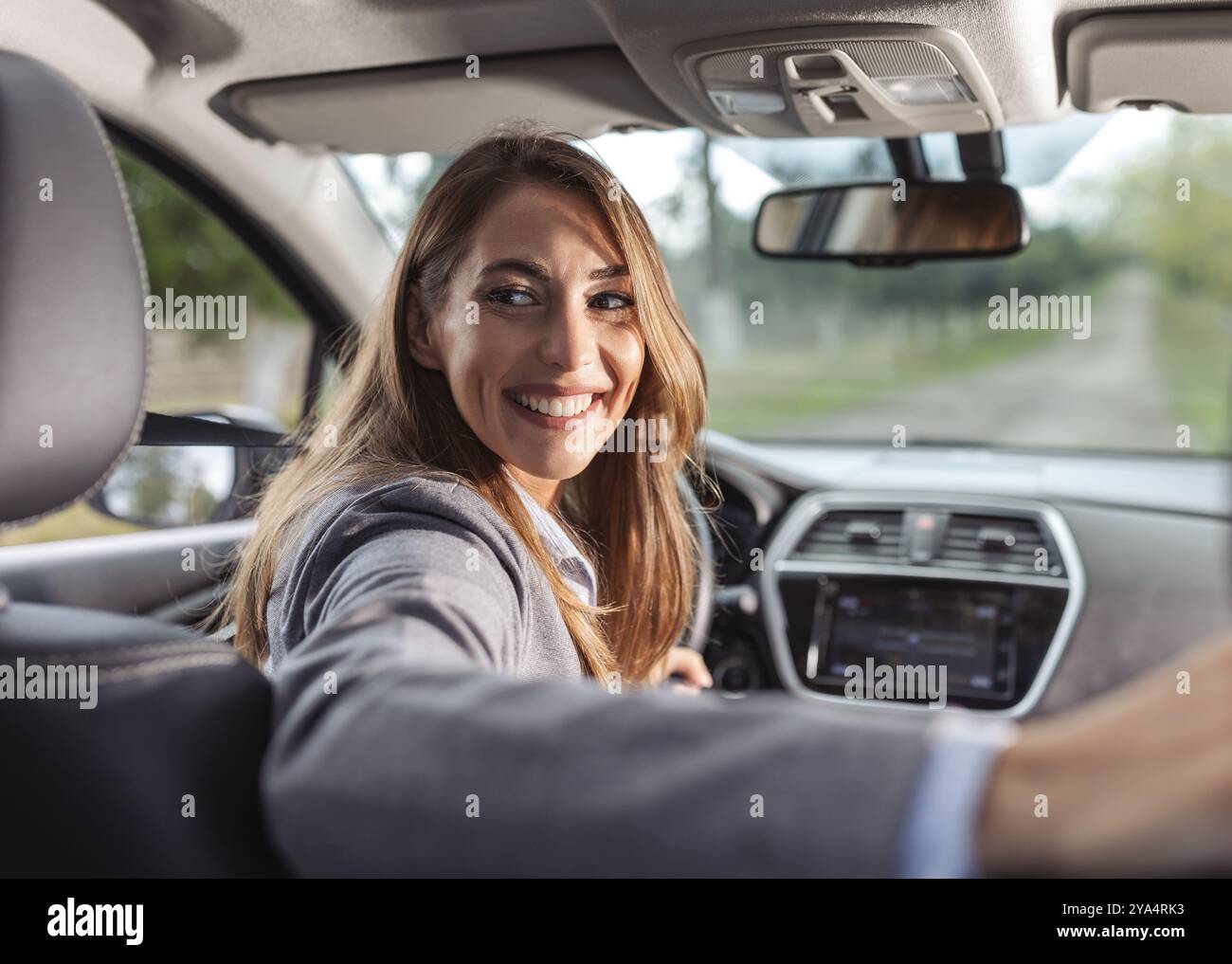 Pretty young woman driving car and looking over shoulder at back ...