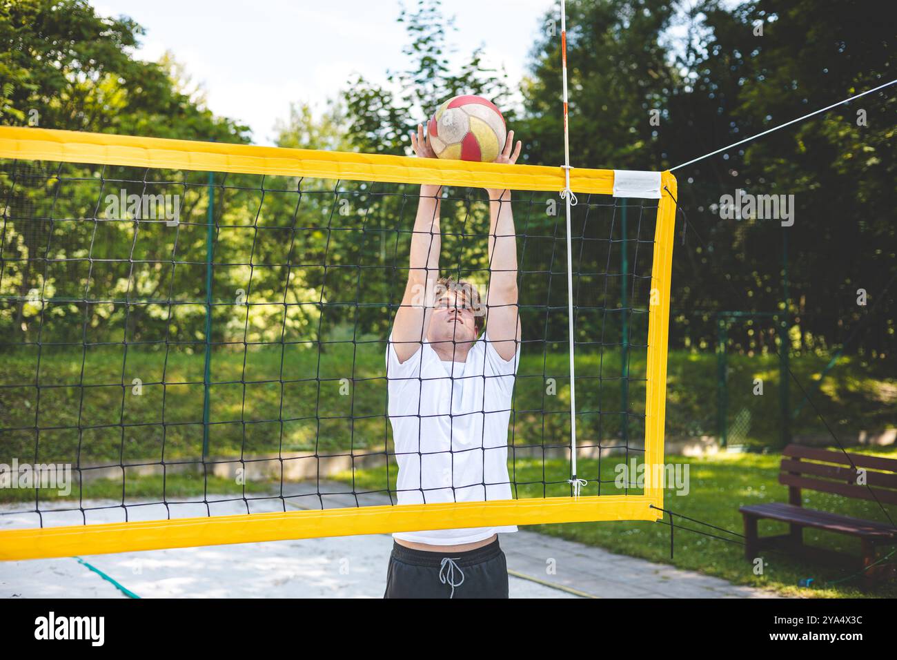 Young man jumps to block a volleyball at the net during a beach ...