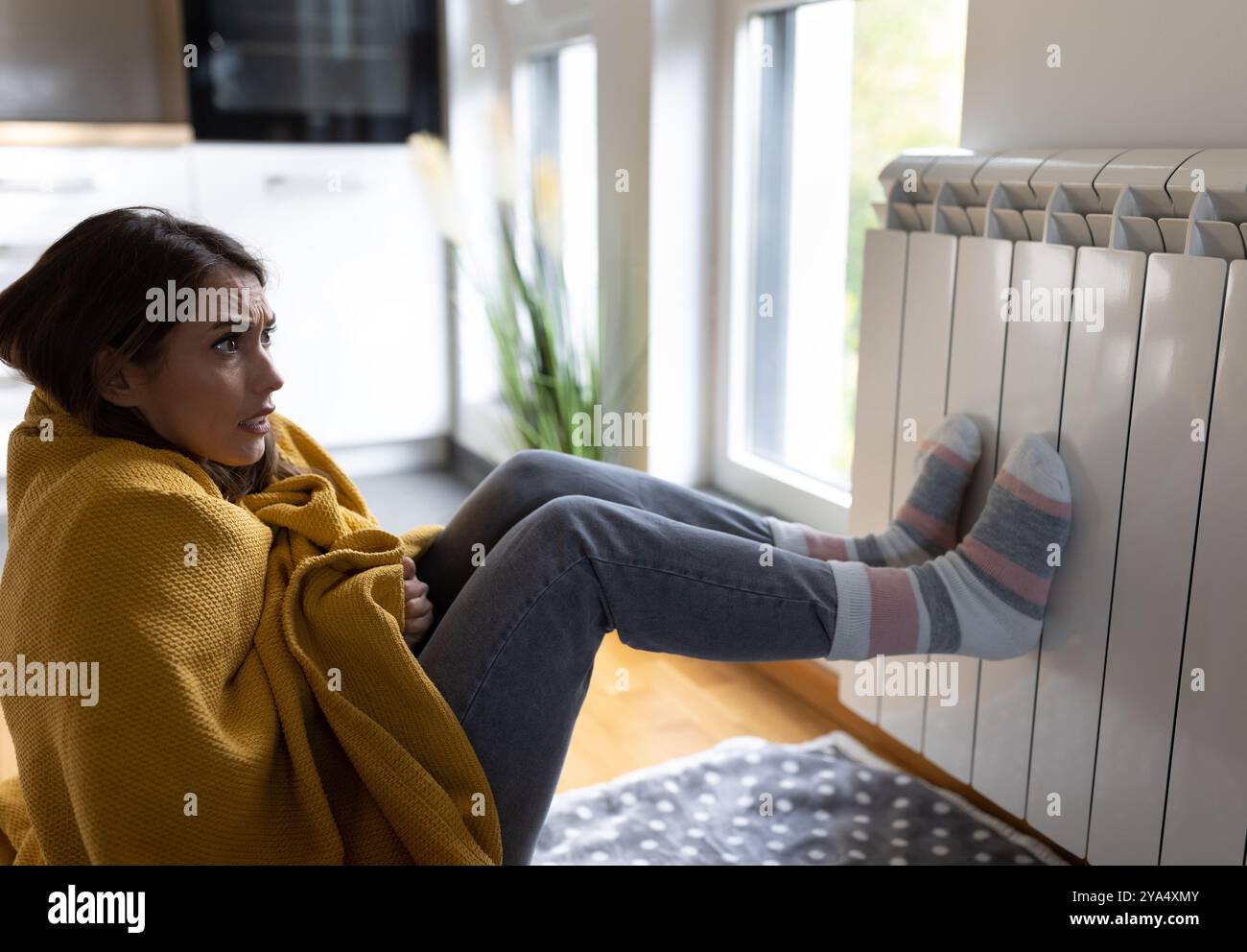 Pretty girl freezing, sitting on floor draped in blanket and warming ...