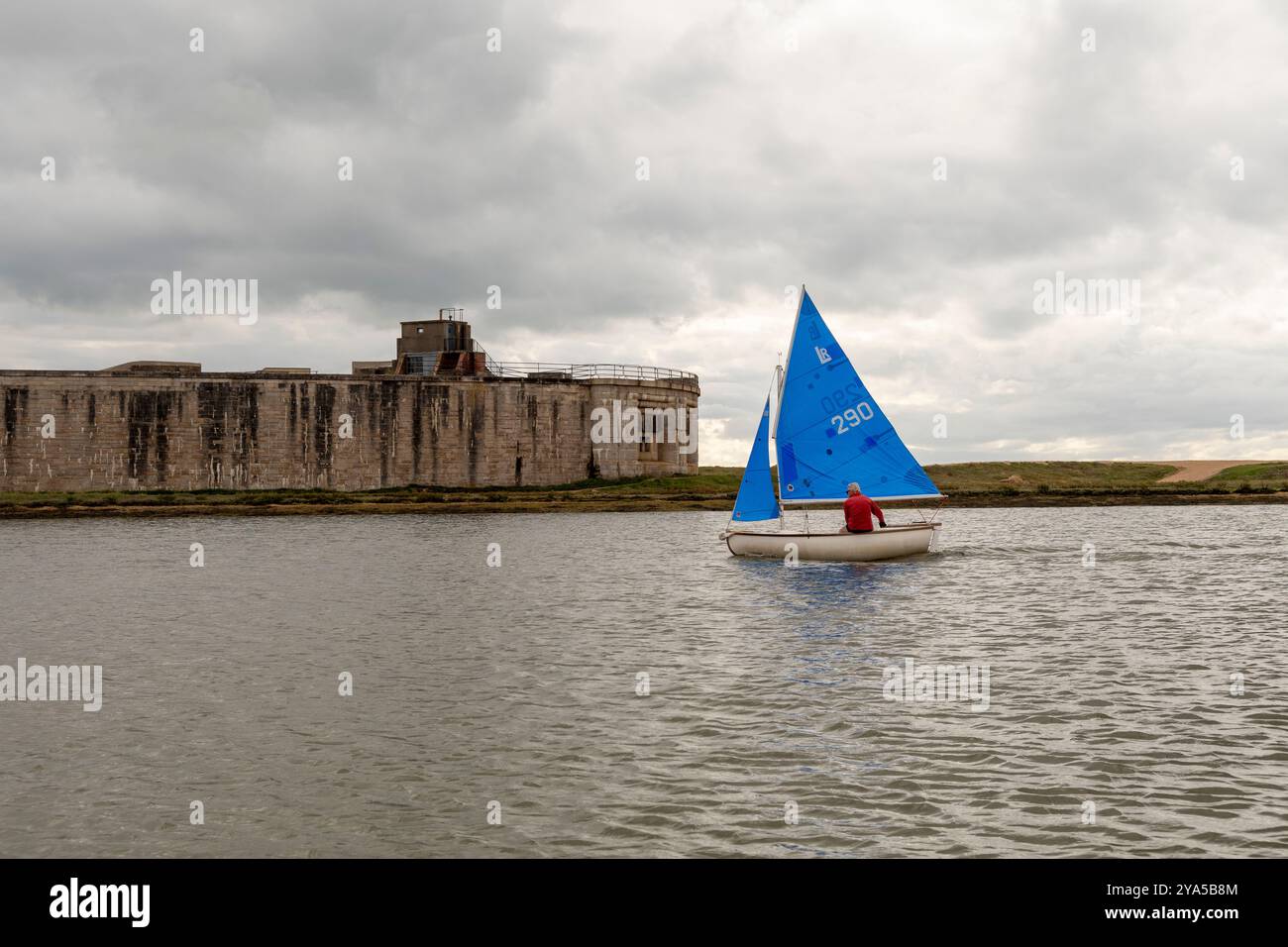 Man sailing dinghy with blue sail past Hurst Castle, Keyhaven ...