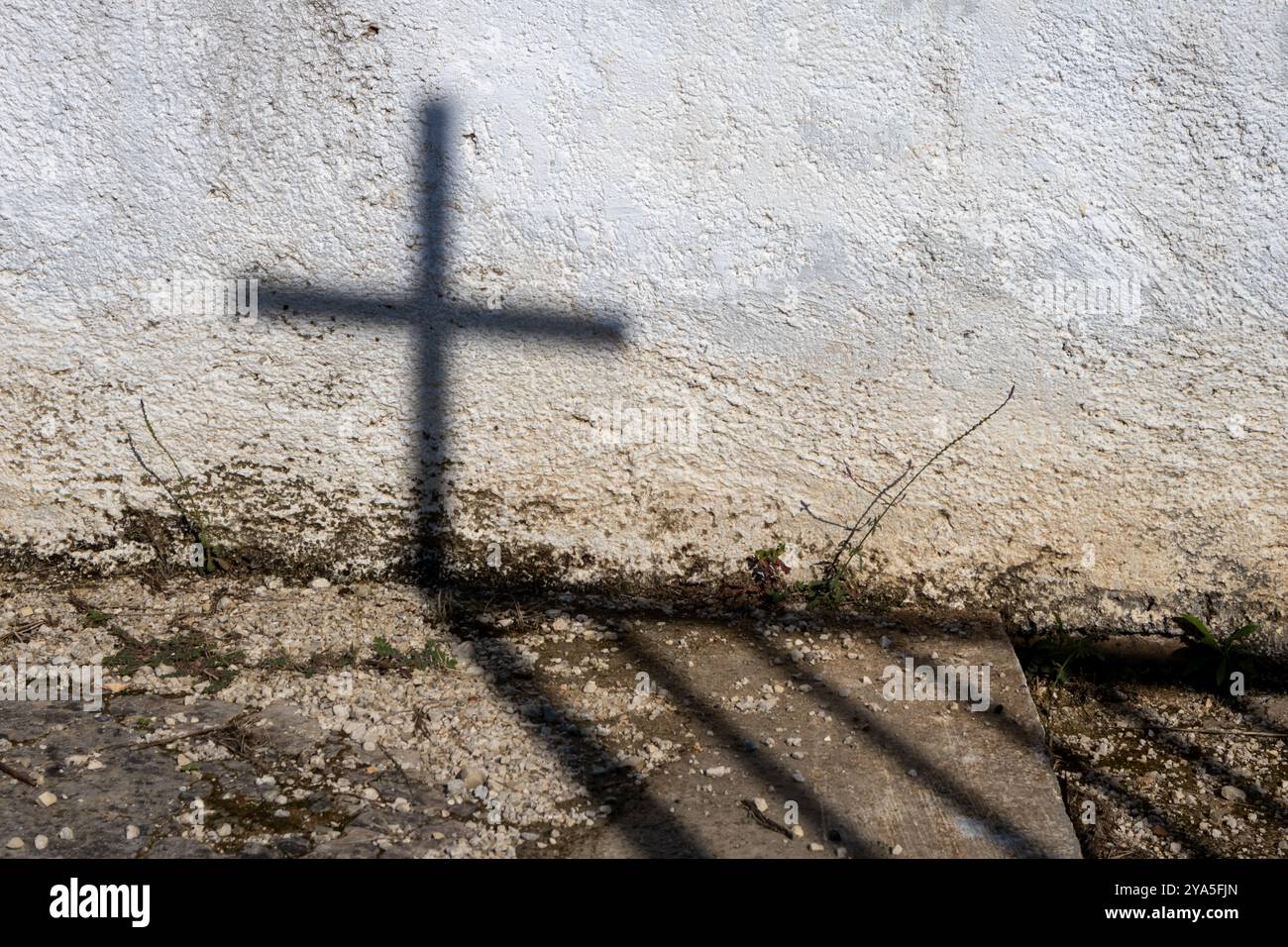 Old weathered wall of a cemetery and a sidewalk. Shadow of a cross on ...