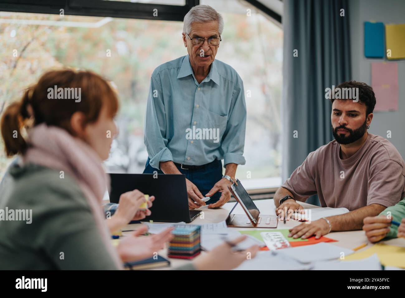 University students collaborating with senior professor on academic ...