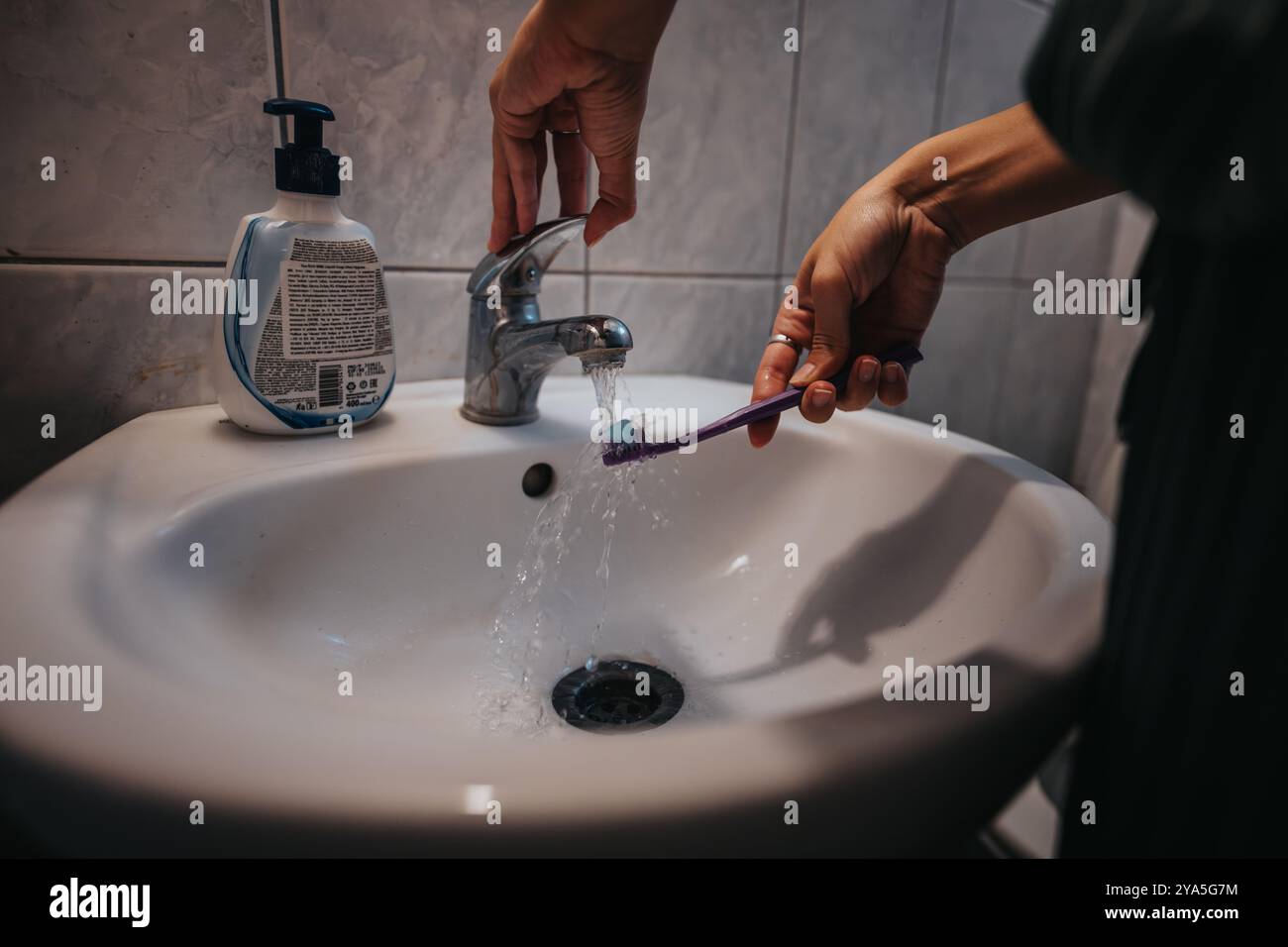 Hand washing toothbrush under running tap water in bathroom Stock Photo ...
