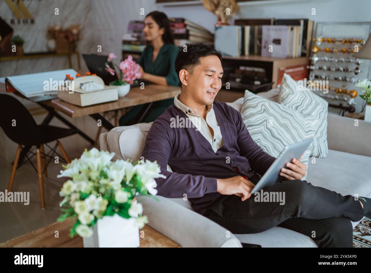 asian male shop owner watching his digital tablet while sitting on sofa ...