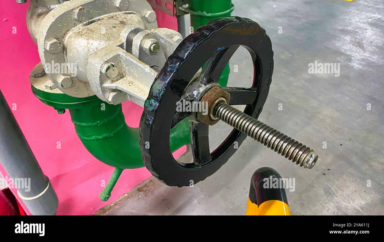 A close-up of a metallic industrial valve with a black wheel handle ...