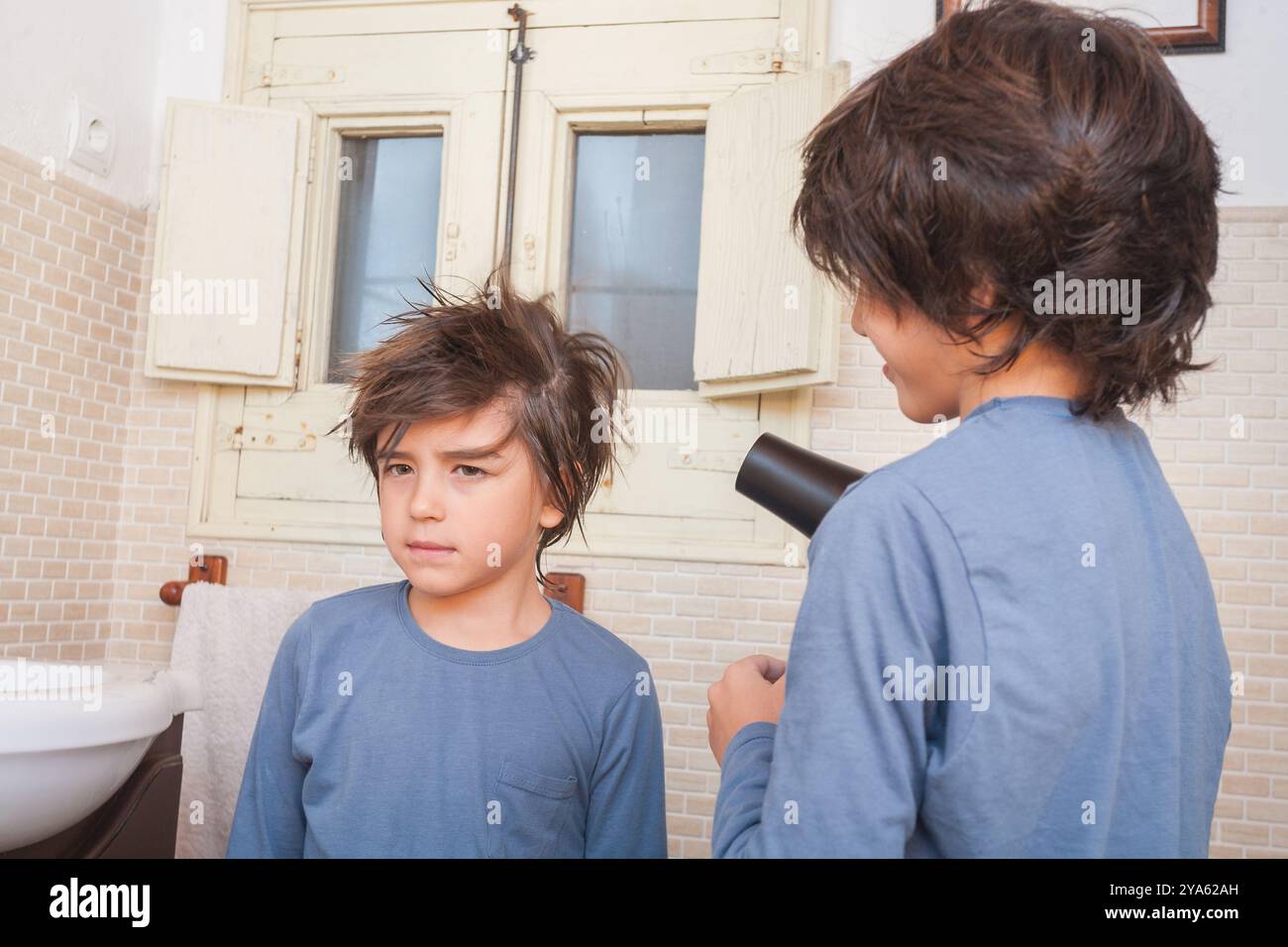 Boy dries his brother's hair with the hairdryer in the bathroom after ...