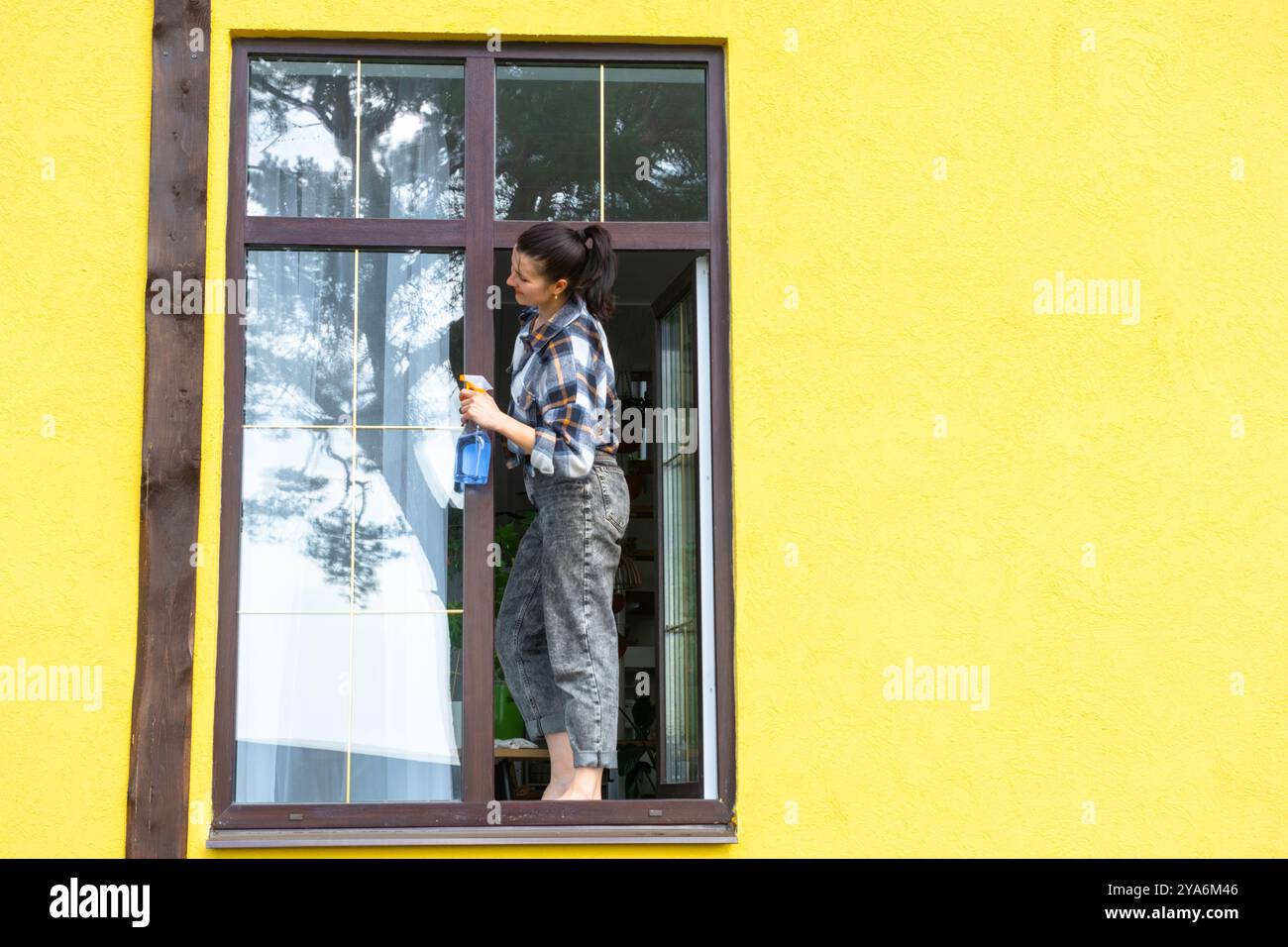 A woman manually washes the window of the house with a rag with a spray ...