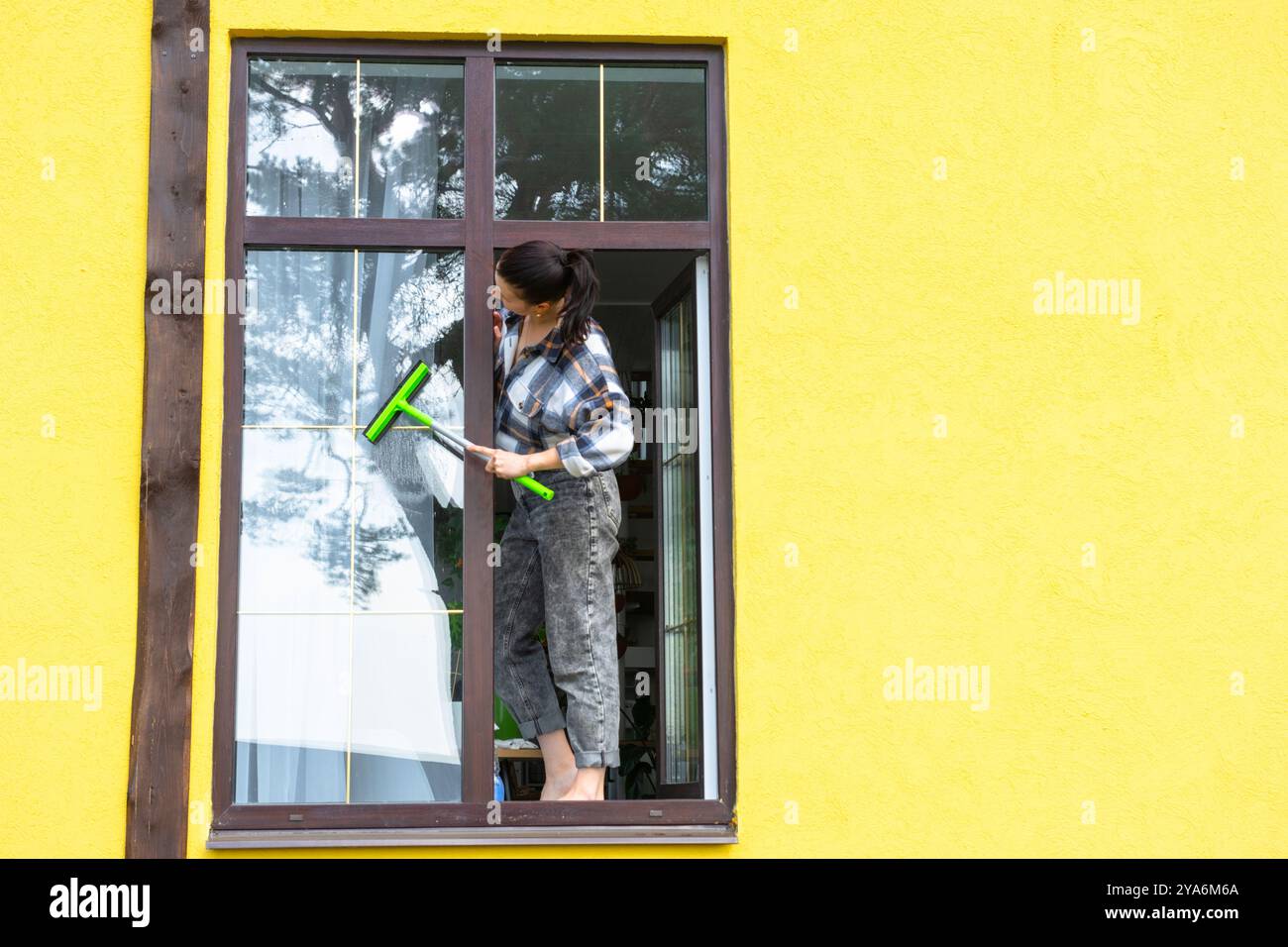 A woman manually washes the window of the house with a rag with a spray cleaner and a mop ...