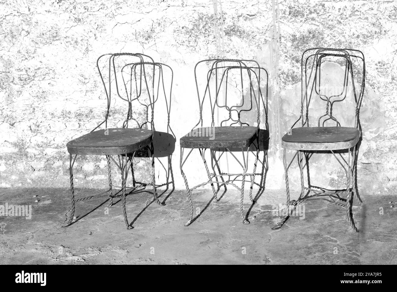 three old rusty metal chairs standing in front of an old wall in India ...