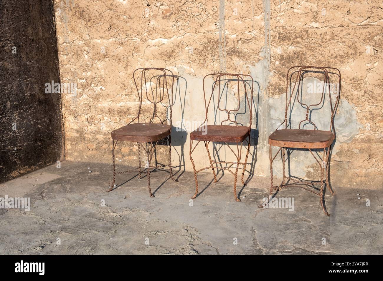 three old rusty metal chairs standing in front of an old wall in India ...