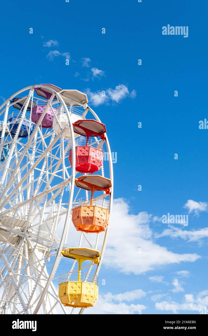 Colourful Ferris wheel set against a bright blue sky with soft clouds ...