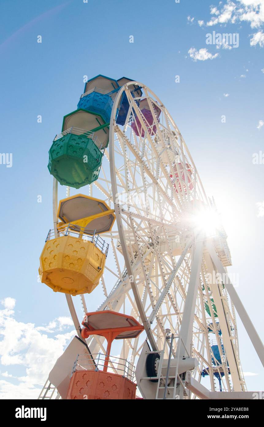 Colourful Ferris wheel set against a bright blue sky with soft clouds ...