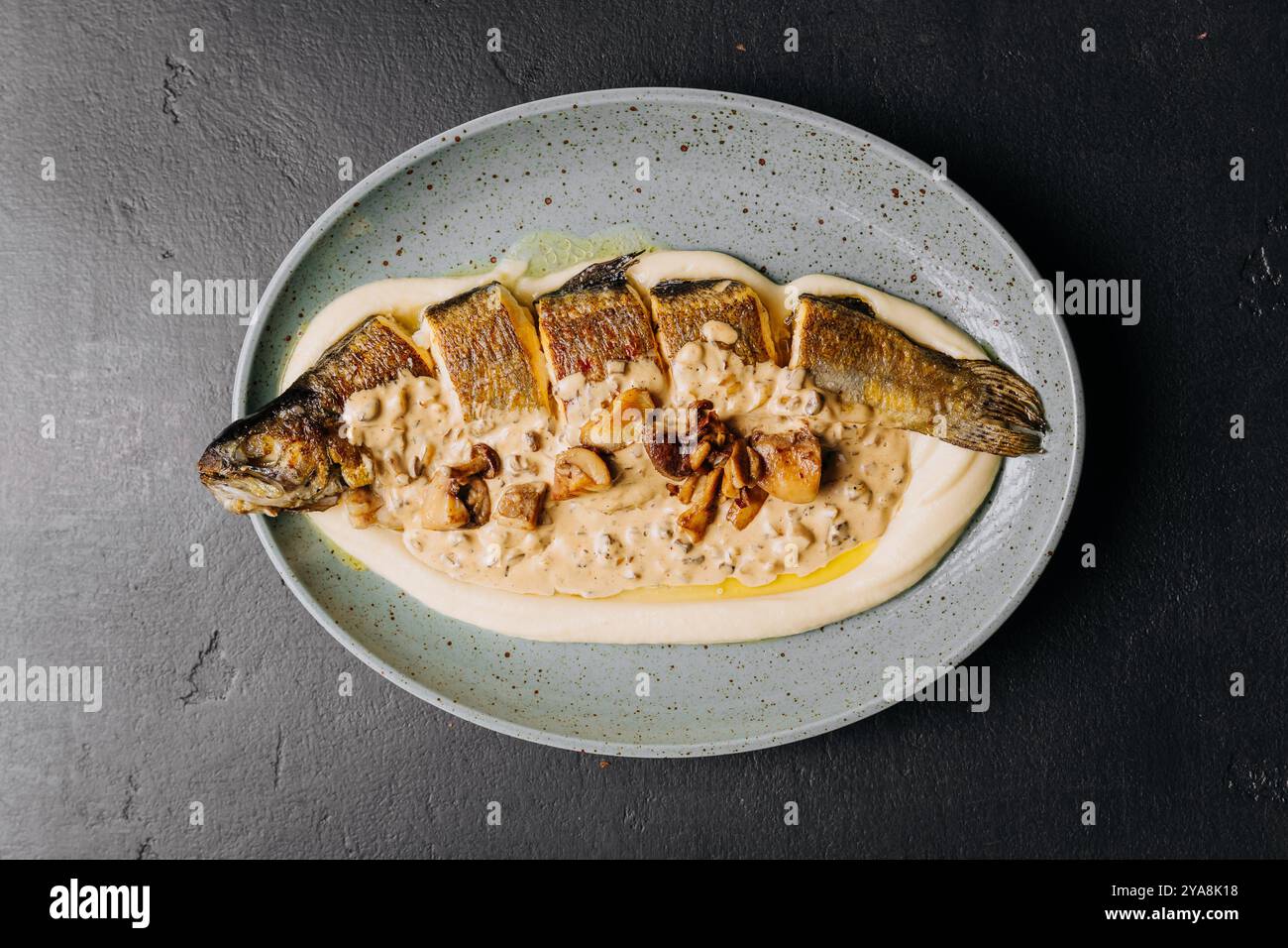 Whole roasted fish with creamy mushroom sauce and mashed potatoes on a ...