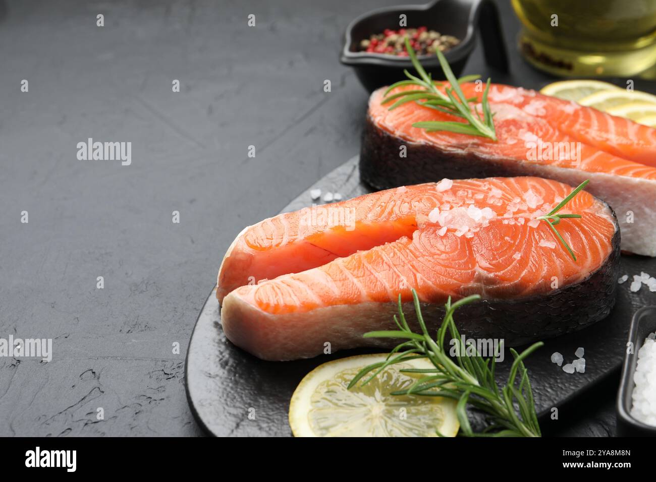 Fresh raw salmon steaks with salt, lemon and rosemary on dark textured ...