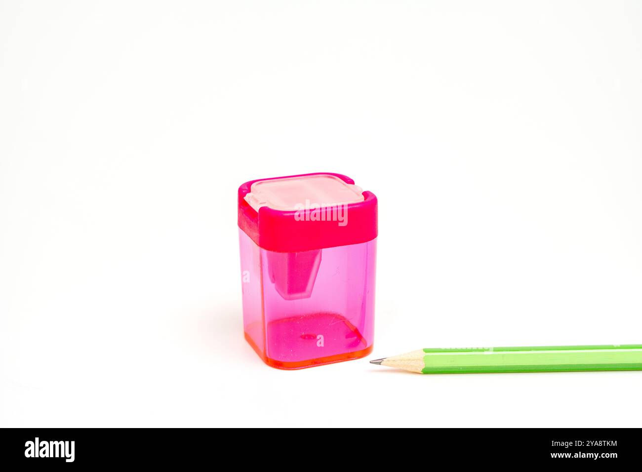 A pink pencil sharpener sits on a white background next to a green ...