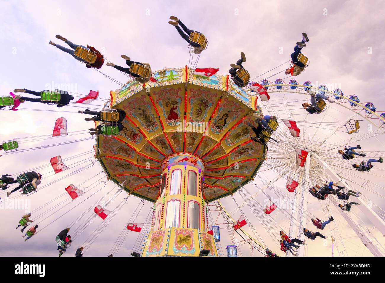 Chain carousel in motion with cheerful people in front of a cloudy sky ...