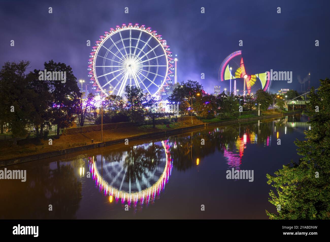 An illuminated Ferris wheel and fairground rides at night, surrounded ...