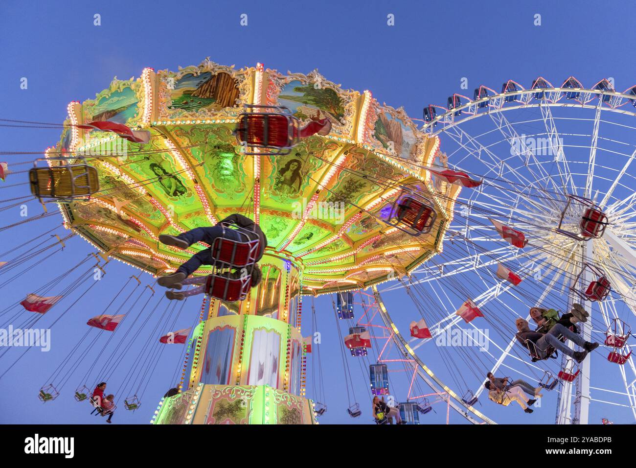 Illuminated chain carousel and Ferris wheel at night with cheerful ...