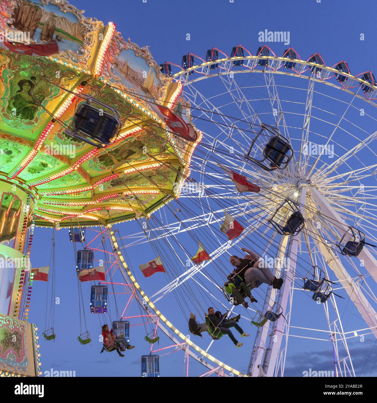 Illuminated chain carousel and Ferris wheel at night with cheerful ...