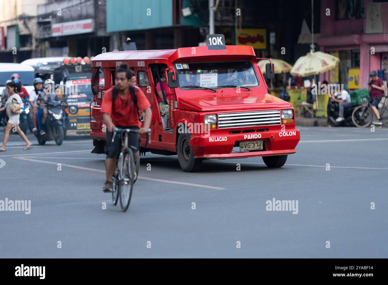 A colorful red Jeepney Multicab weaves through bustling Colon Street in ...