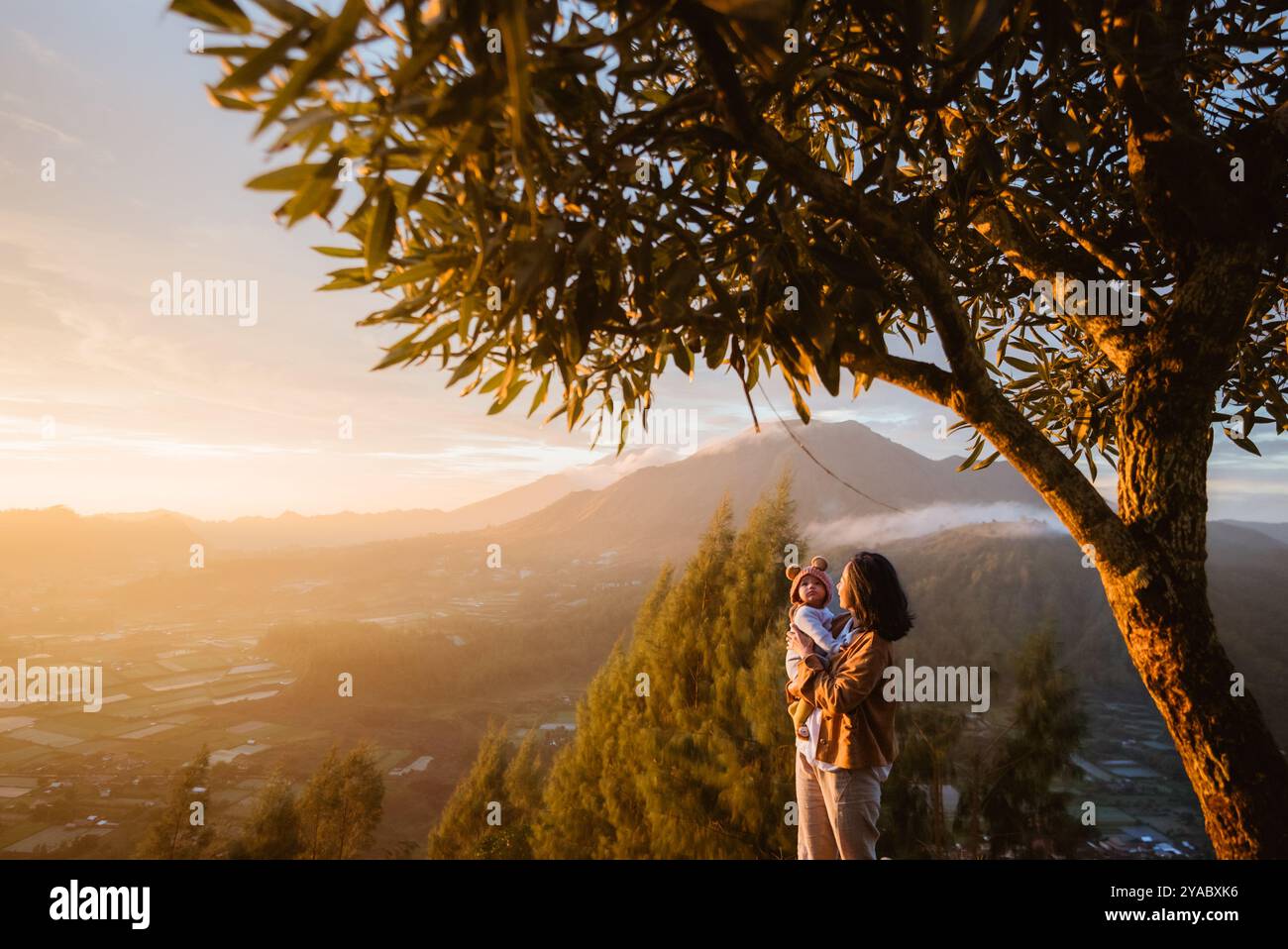 A woman holds a baby in her arms standing under a tree Stock Photo - Alamy