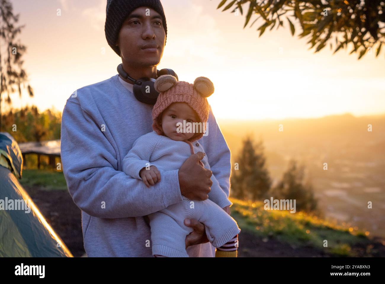A man cradles a baby in his arms before a beautiful sunset Stock Photo ...