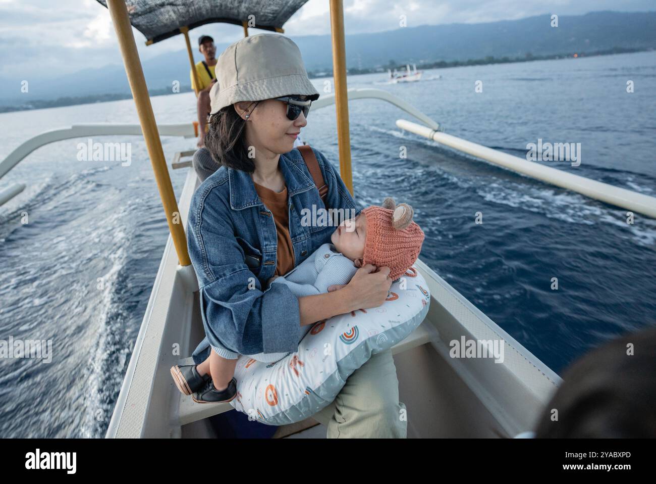 A woman is gently holding a baby on a small boat in the vast ocean ...