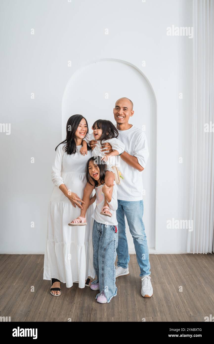 A cheerful family is posing happily for a picture in front of a white ...