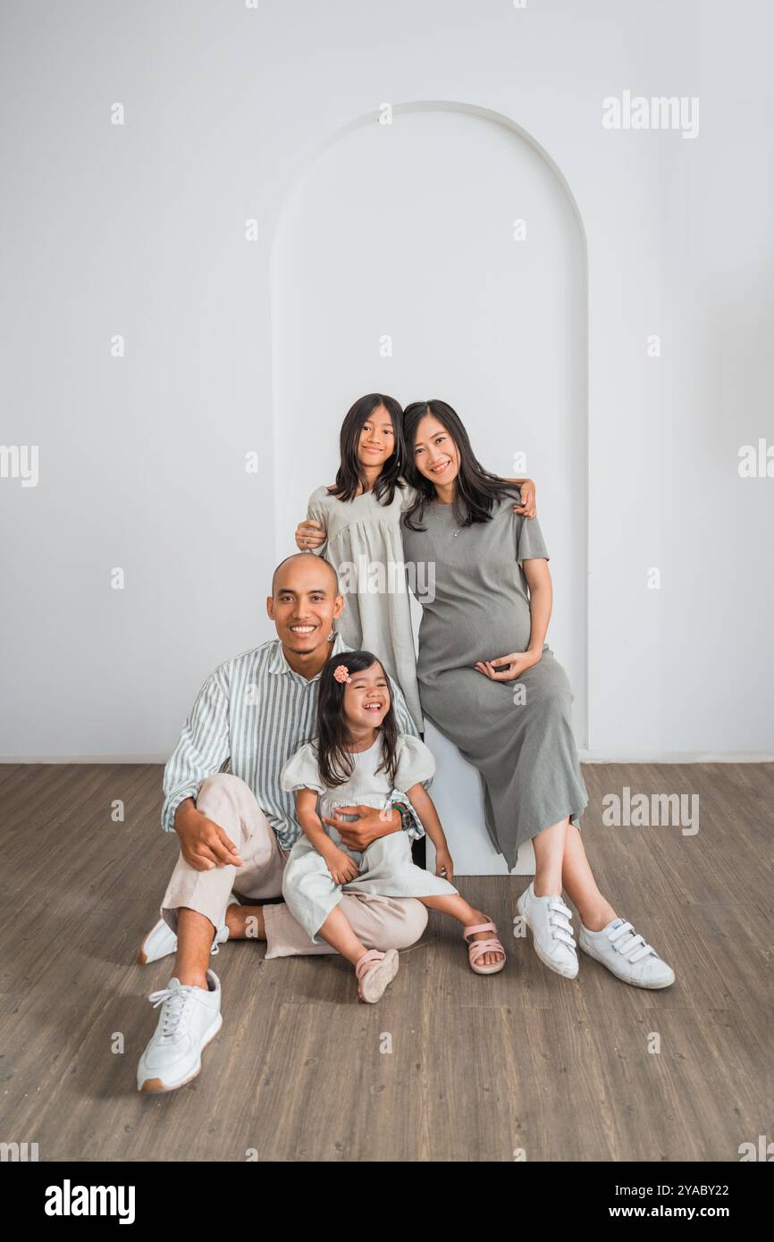 A family is sitting comfortably on the floor, posing for a picture ...