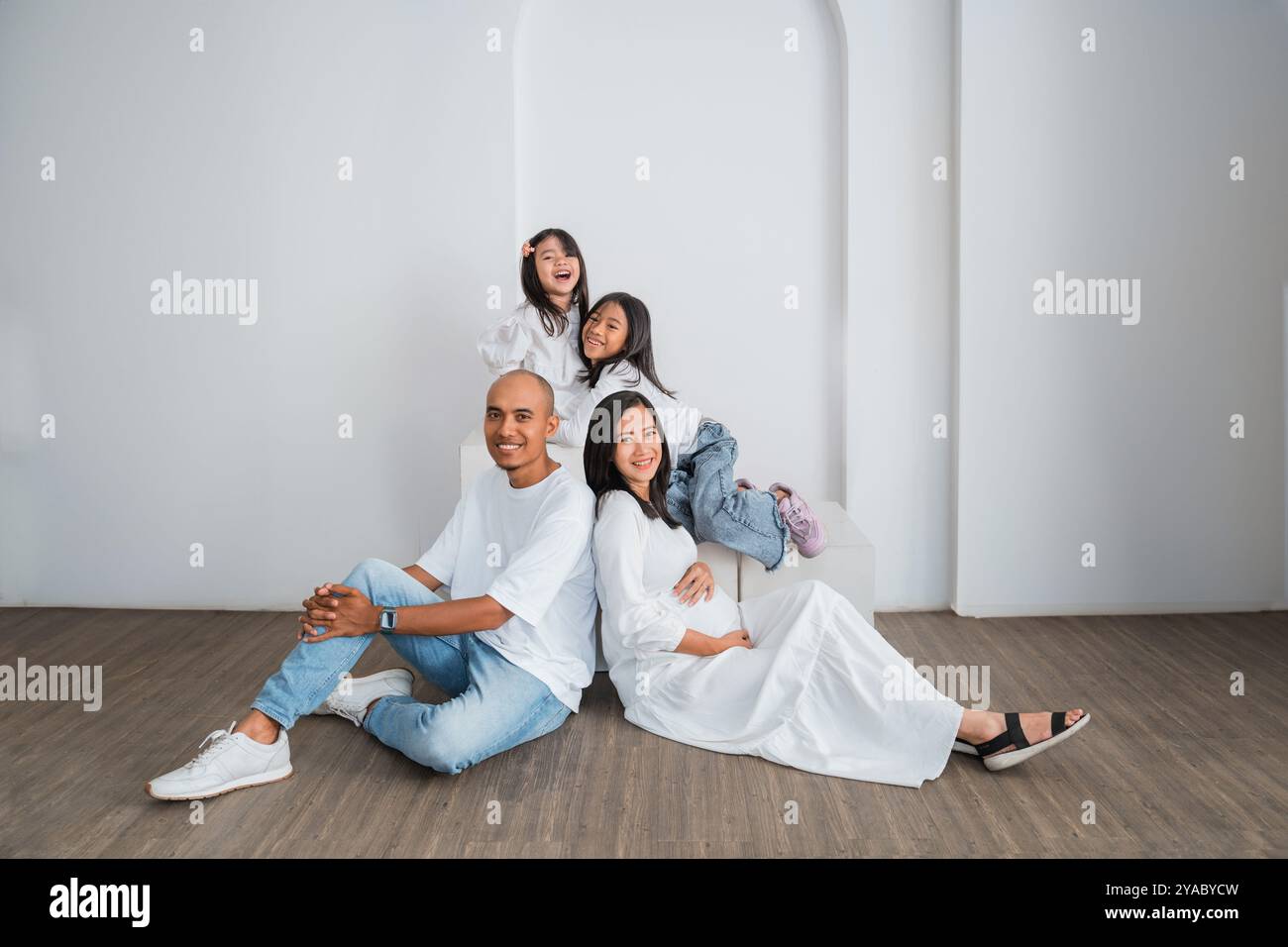 A family is comfortably sitting on the floor while posing for a picture ...